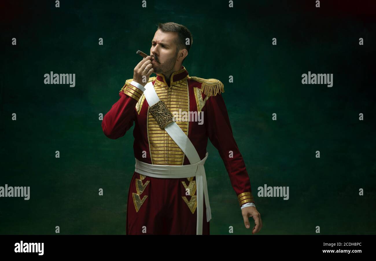 Smoking cigarette. Young man in suit as Nicholas II isolated on dark ...
