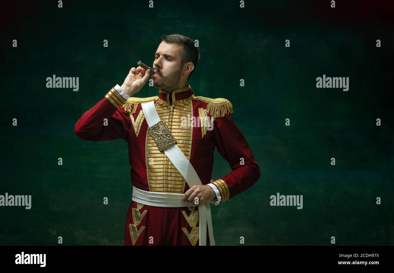 Smoking cigarette. Young man in suit as Nicholas II isolated on dark ...