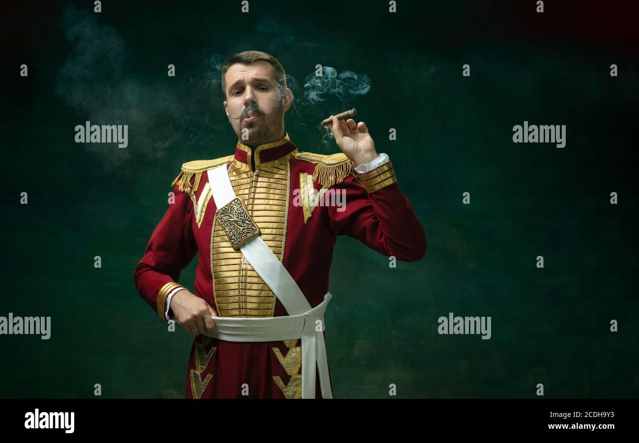 Smoking cigarette. Young man in suit as Nicholas II isolated on dark ...