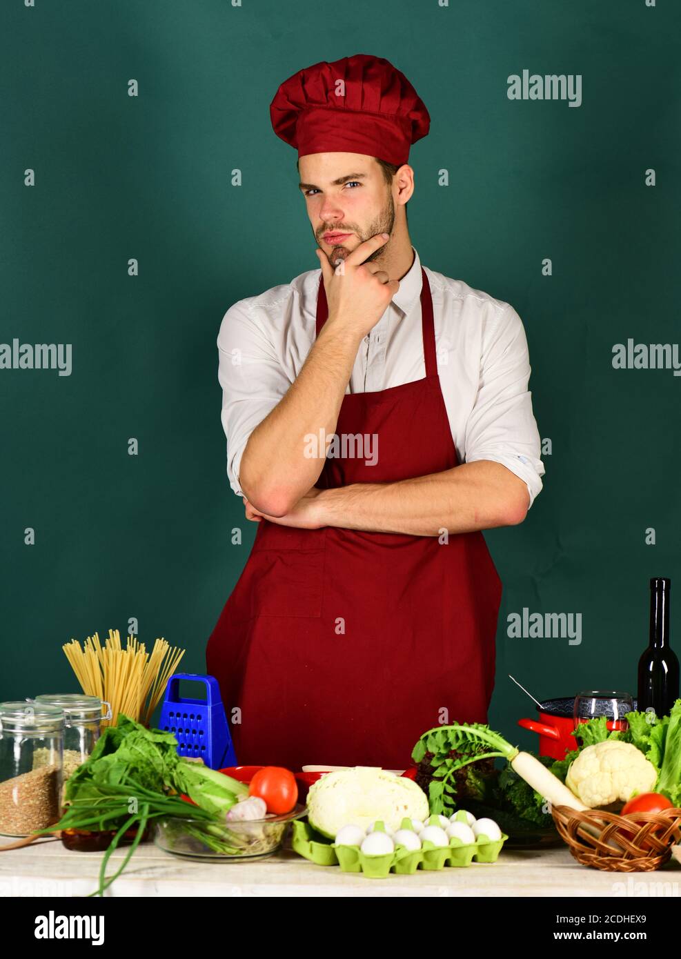 Cook or chef with thoughtful face stands by vegetables and tools on ... Cook or chef with thoughtful face stands by vegetables and tools on ...