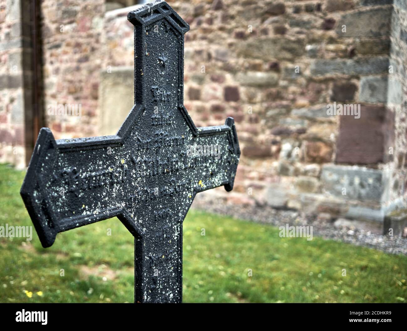 Medieval cast-iron cross with the wall of a stone church with ...