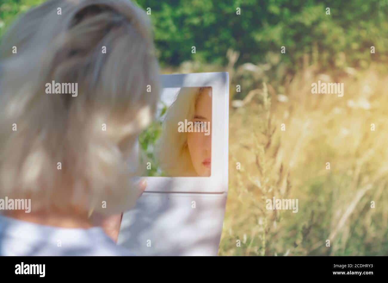 Blonde woman looking in the mirror on nature. View from behind Stock ...