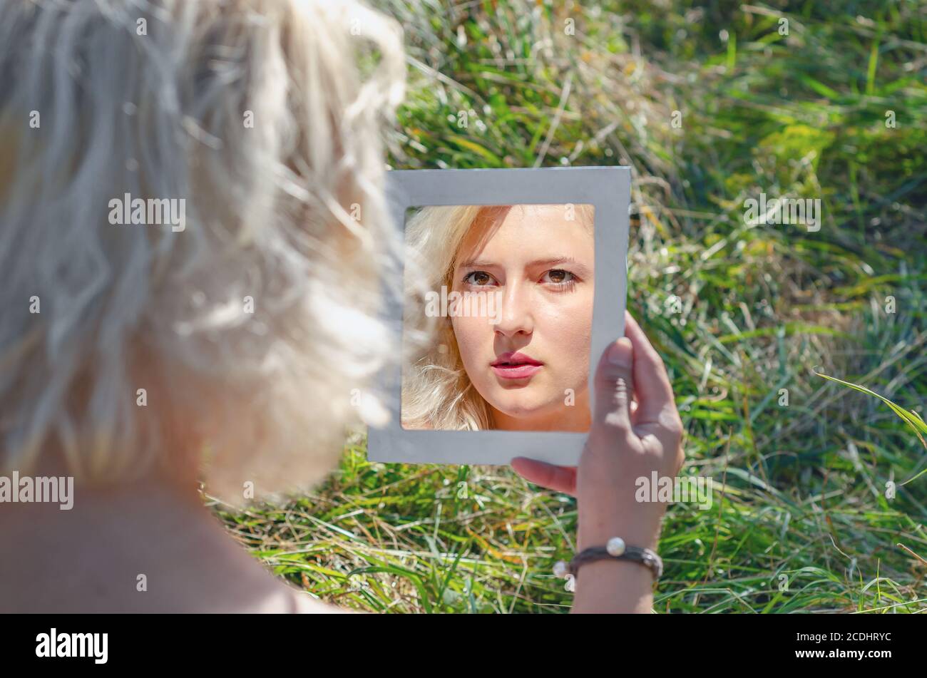 Blonde woman looking in the mirror on nature. View from behind Stock ...