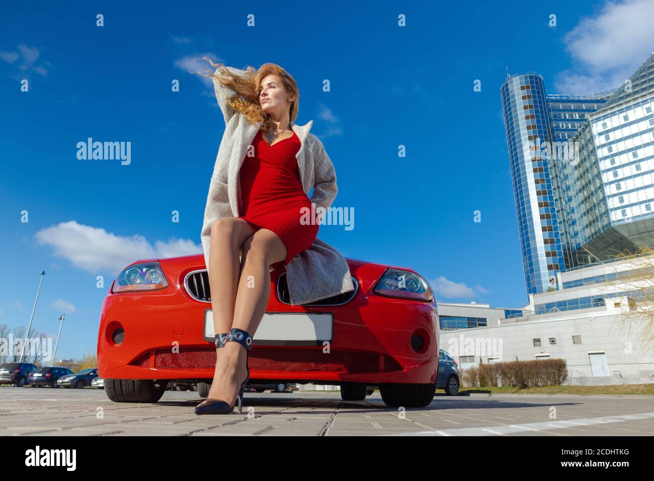 Beautiful blonde woman in a red dress posing in a red car in the city ...