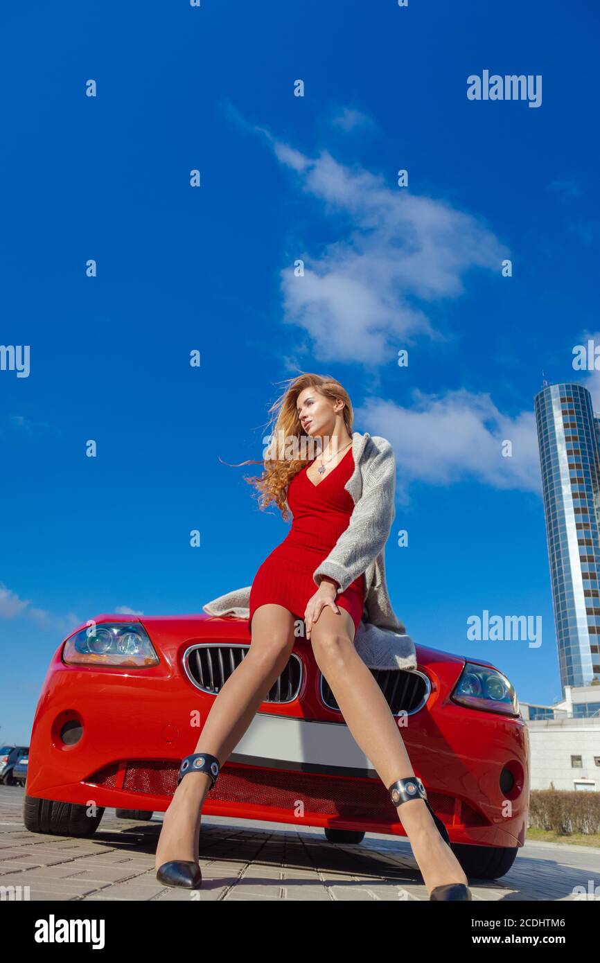 Beautiful blonde woman in a red dress posing in a red car in the city ...