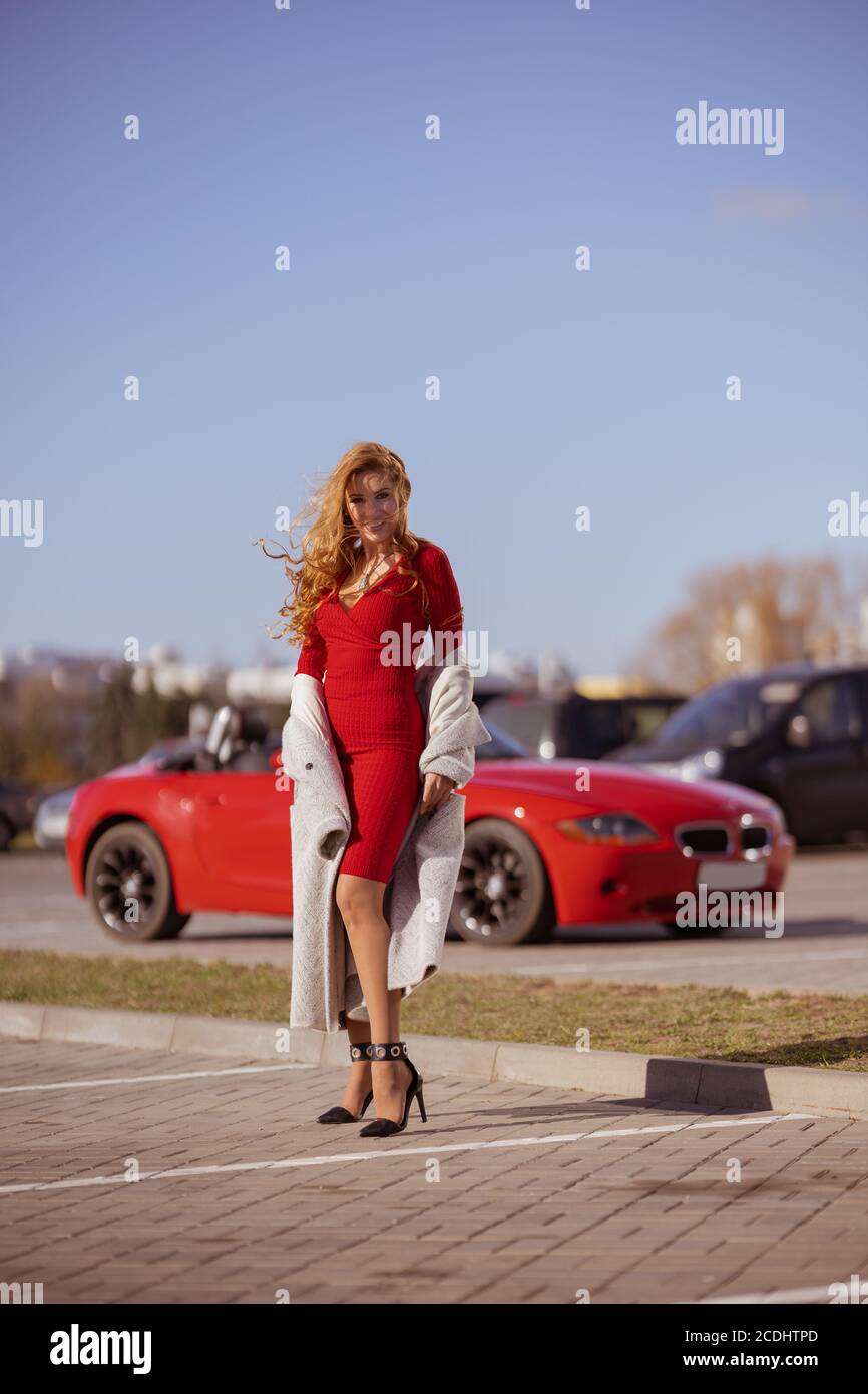 Beautiful blonde woman in a red dress posing in a red car in the city ...