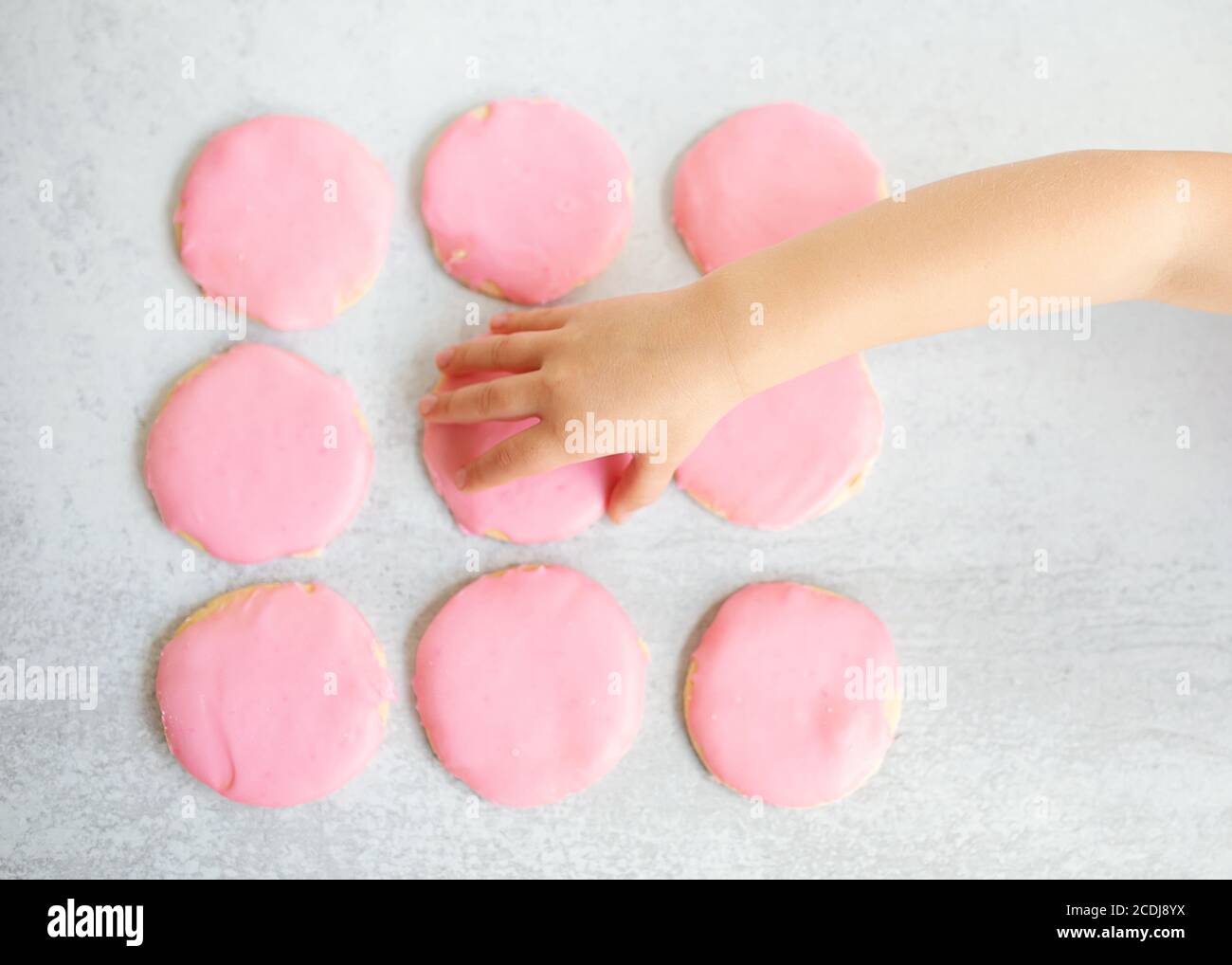 top view child's hand grabbing pink sugar cookie off of table Stock ...