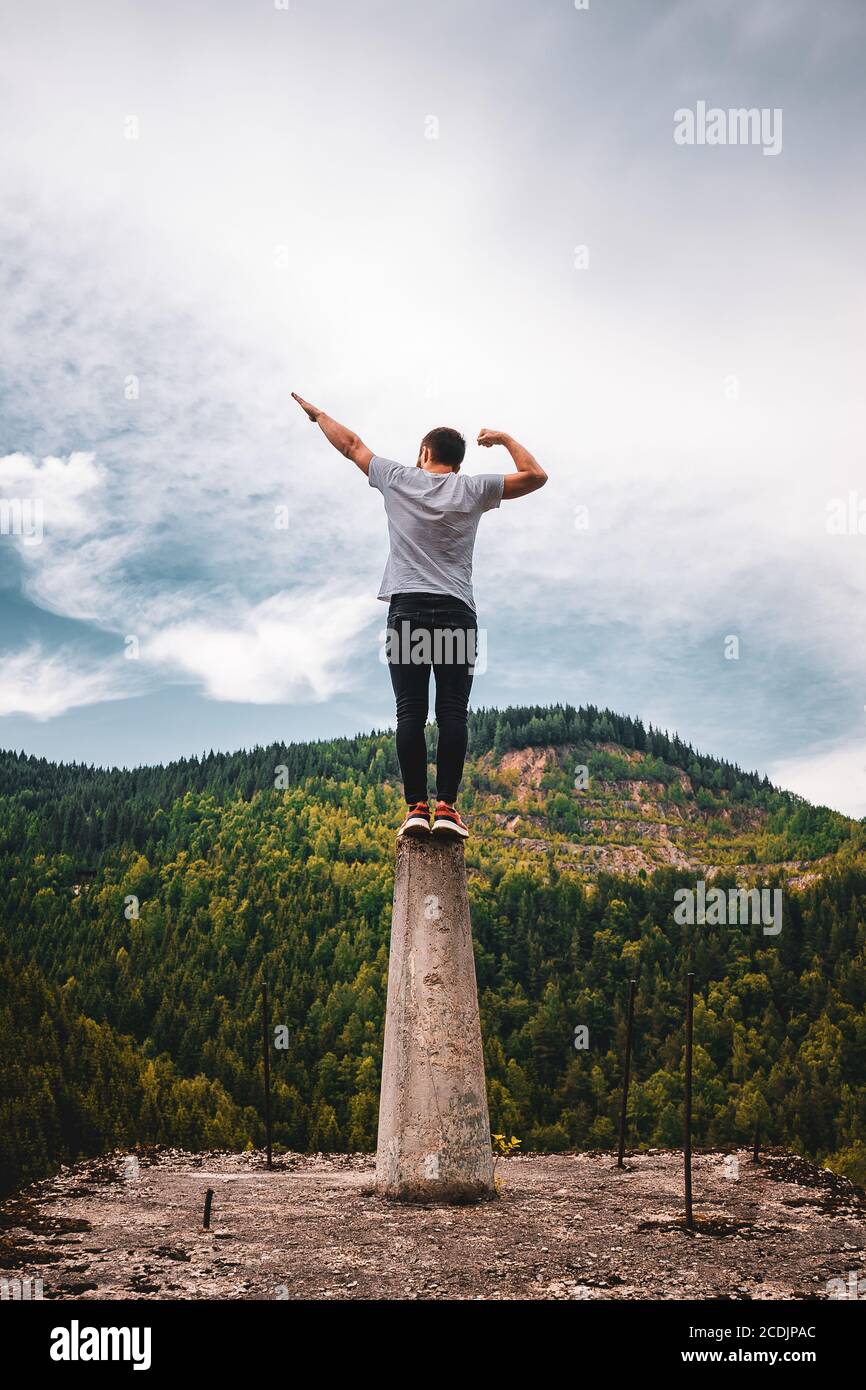 Vertical shot of a young male posing on a platform surrounded by hills ...