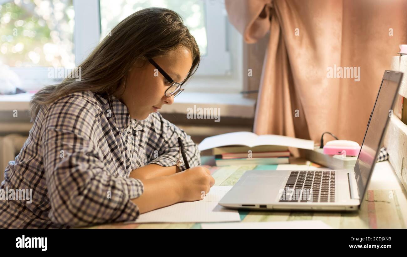 Schoolgirl learns online using a laptop while sitting at home. Remote ...
