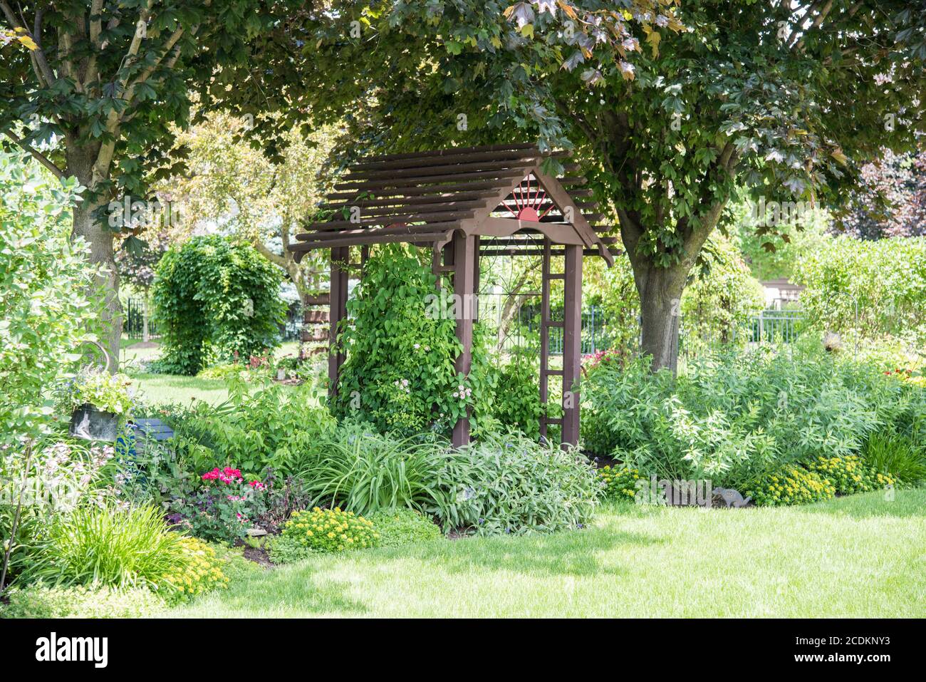 Back yard garden with wooden arbor and flowering plants with deciduous ...