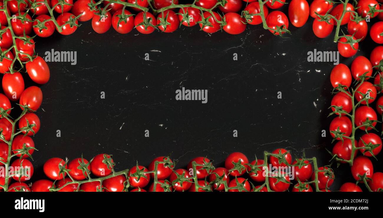 Border frame made out of tomatoes with green vine leaves, empty space ...