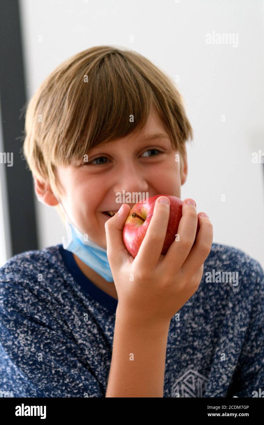 Boy wearing a medical mask eating an apple at school, new normal back ...