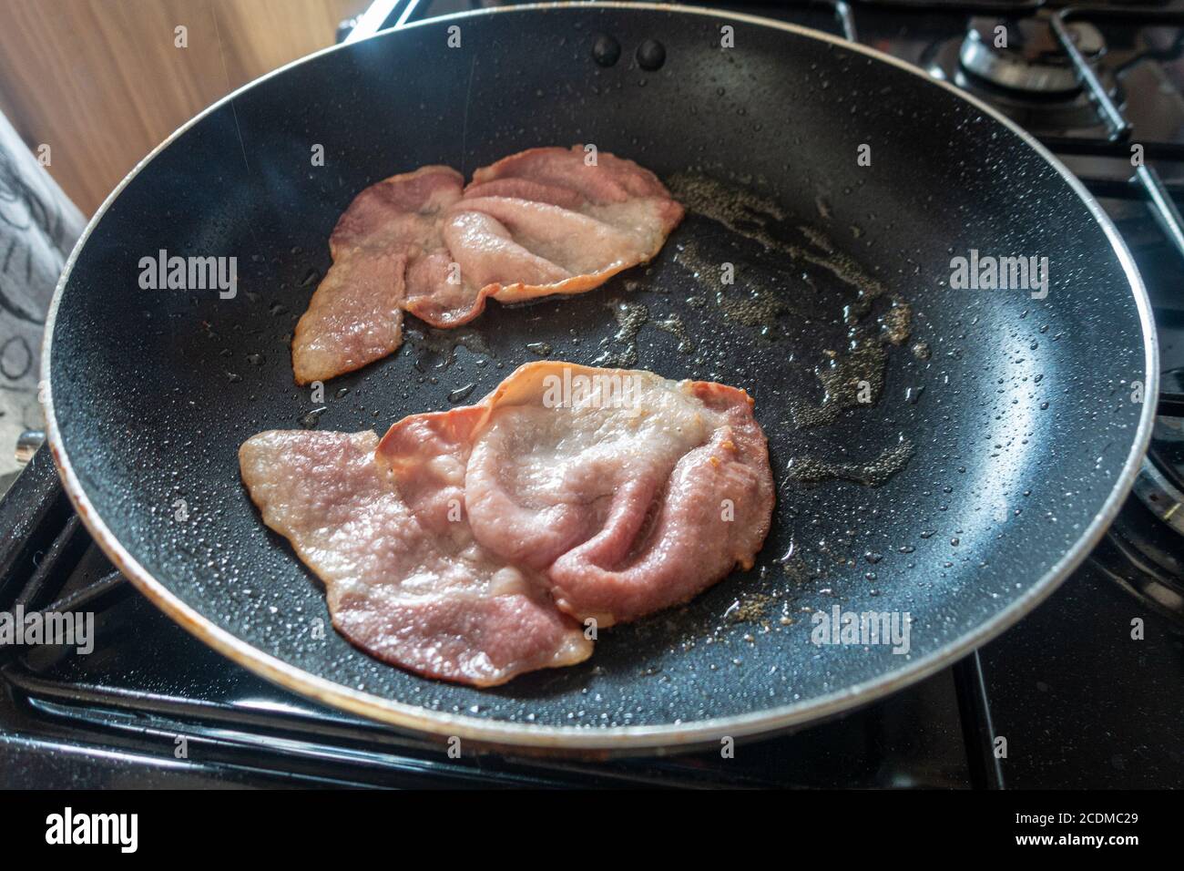 A couple of rashers of bacon cooking in a frying pan Stock Photo - Alamy