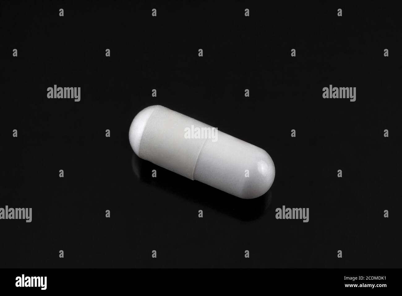 single white capsule pill on a black background with reflection and copy space Stock Photo - Alamy
