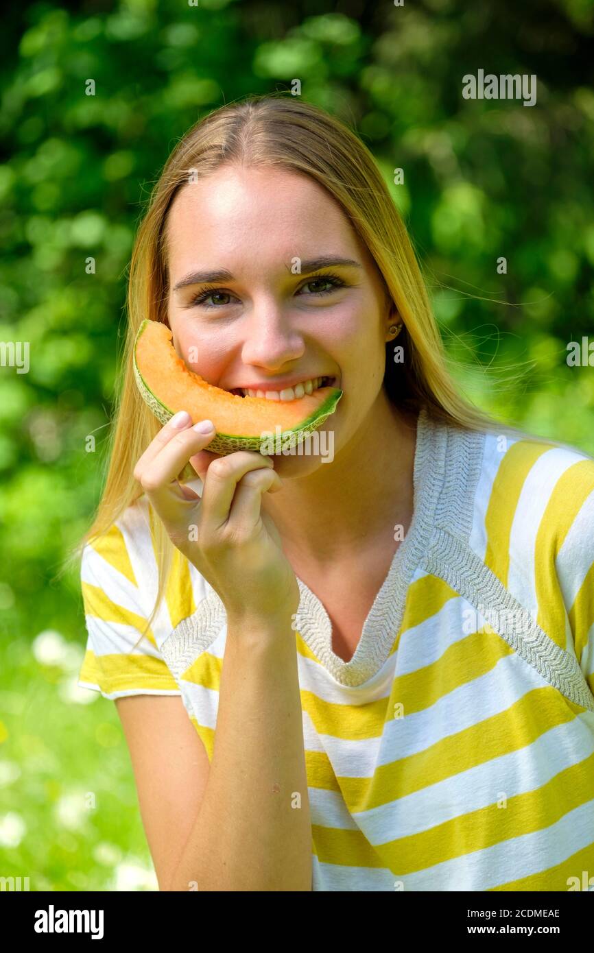 Portrait young blonde woman, biting into a melon, fruit, summer ...