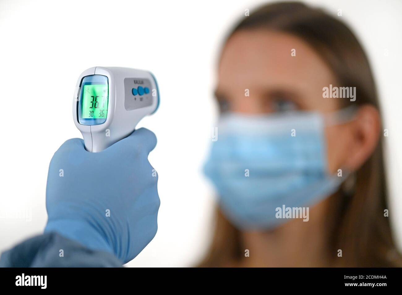 Temperature measurement with forehead thermometer, woman with face mask ...