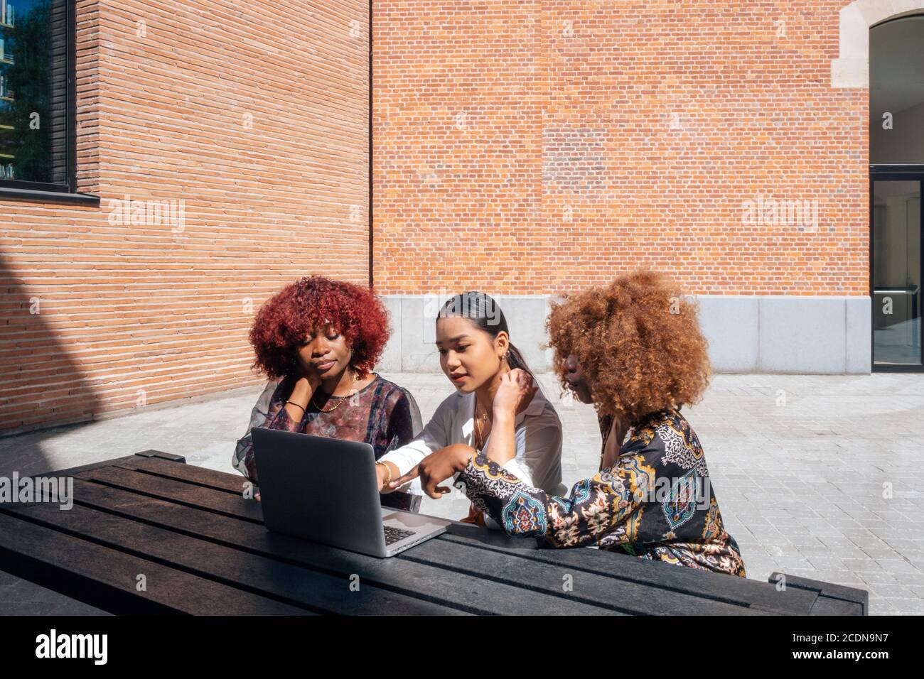 multiracial girls students sitting outdoor the university using a ...