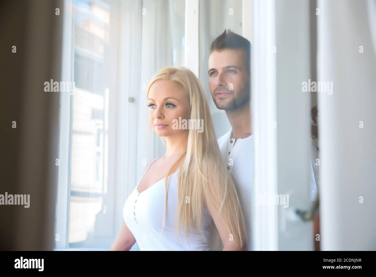 Beautiful young couple standing at the window Stock Photo - Alamy