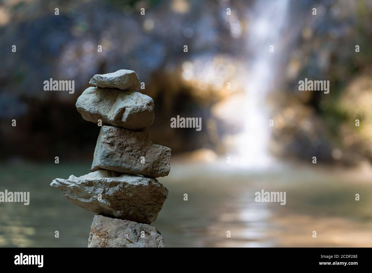 Stacked pile of stones in front of reflecting lake and cascade. Scenie ...