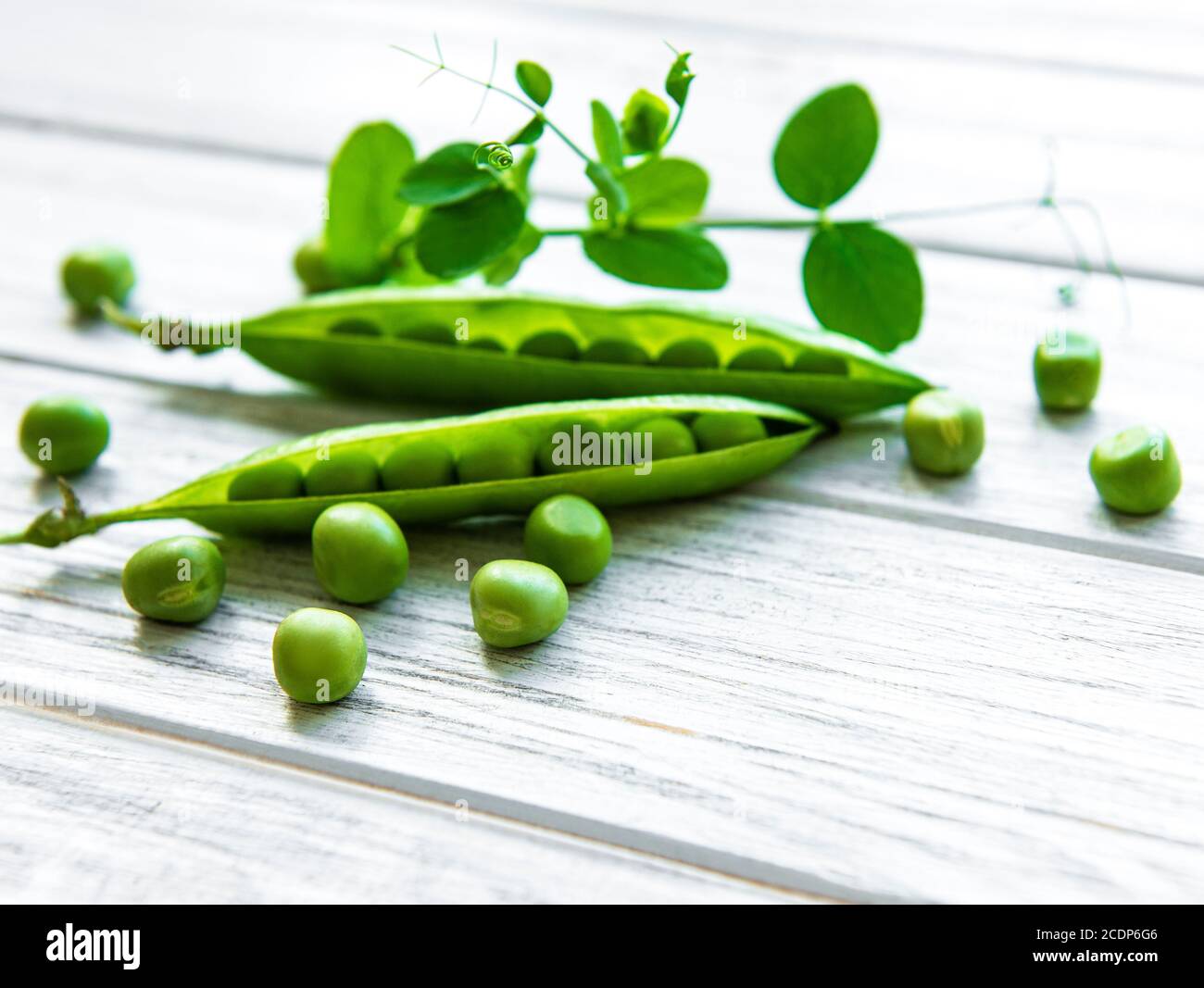 Pods of green peas with pea leaves on a white wooden background ...