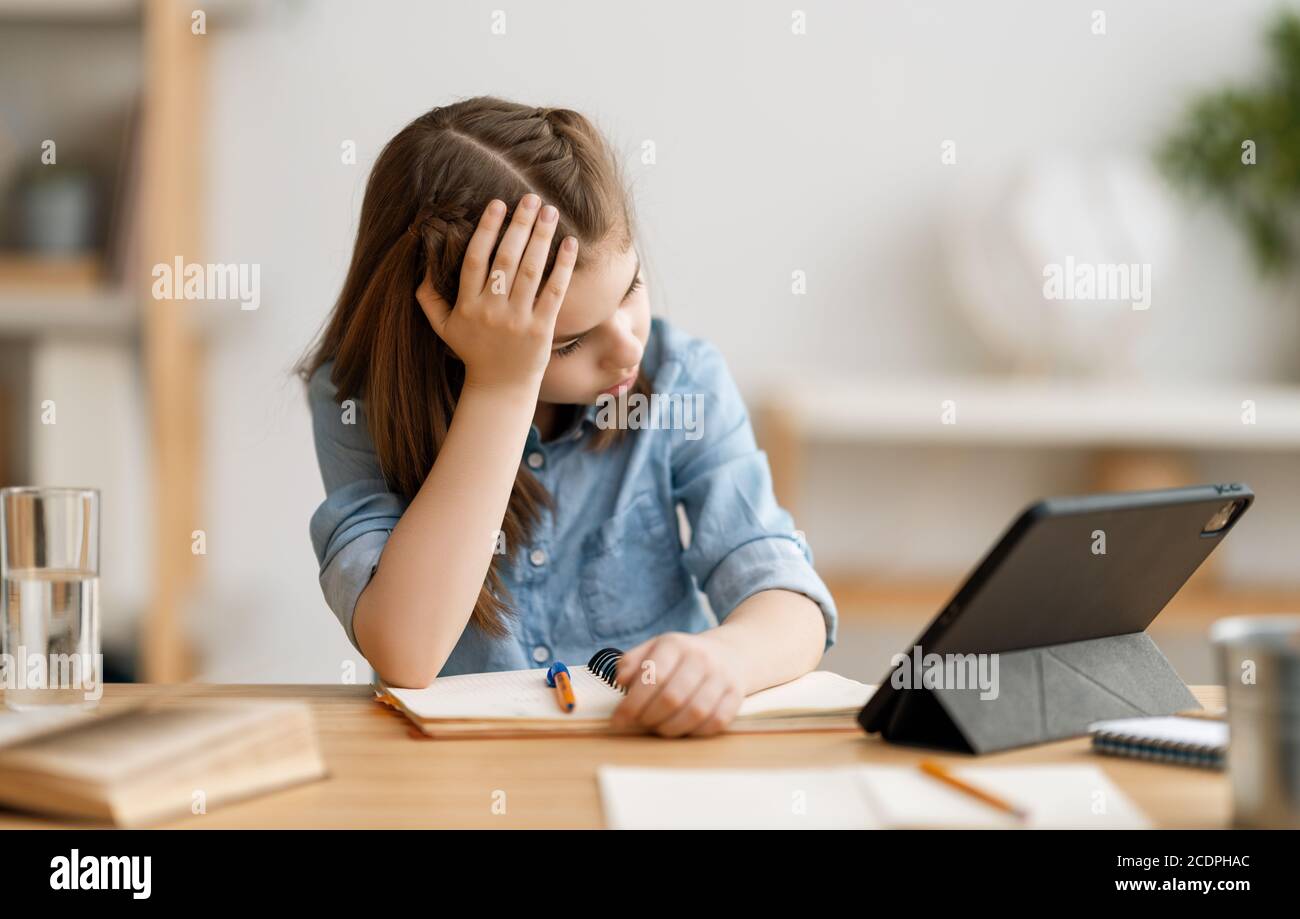 Back to school. Unhappy child is sitting at desk. Girl doing homework ...