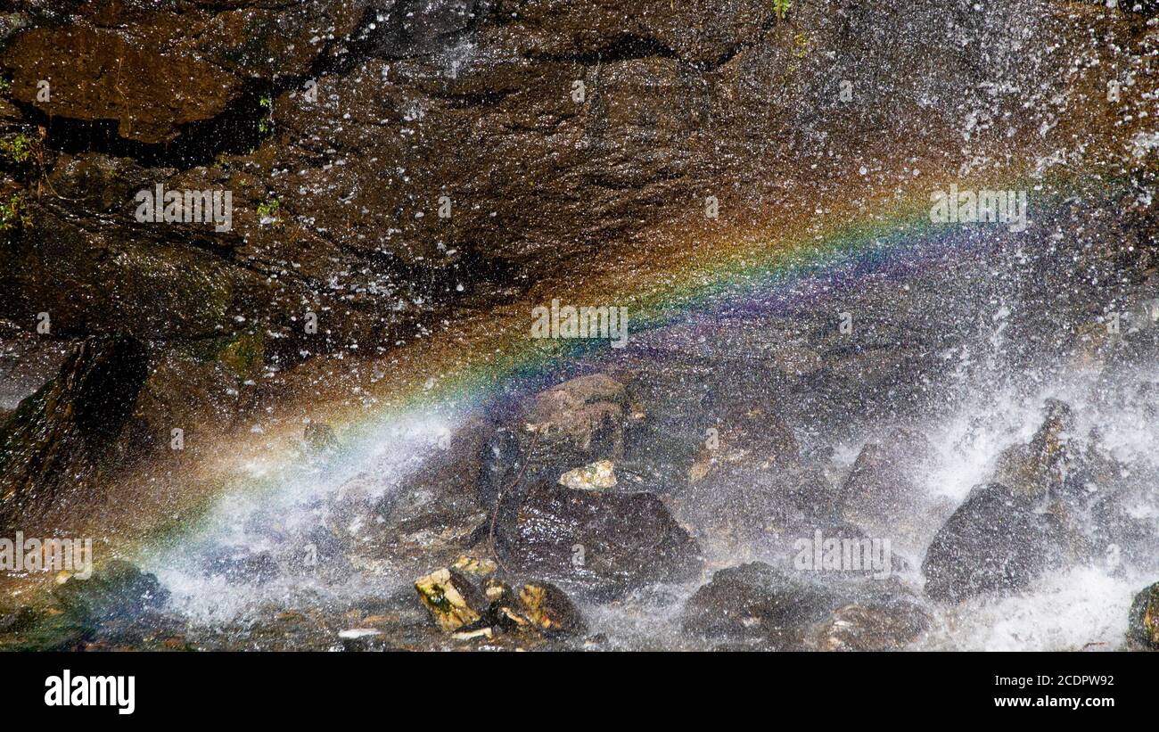 A beautiful rainbow forms under a waterfall due to sunlight passing ...