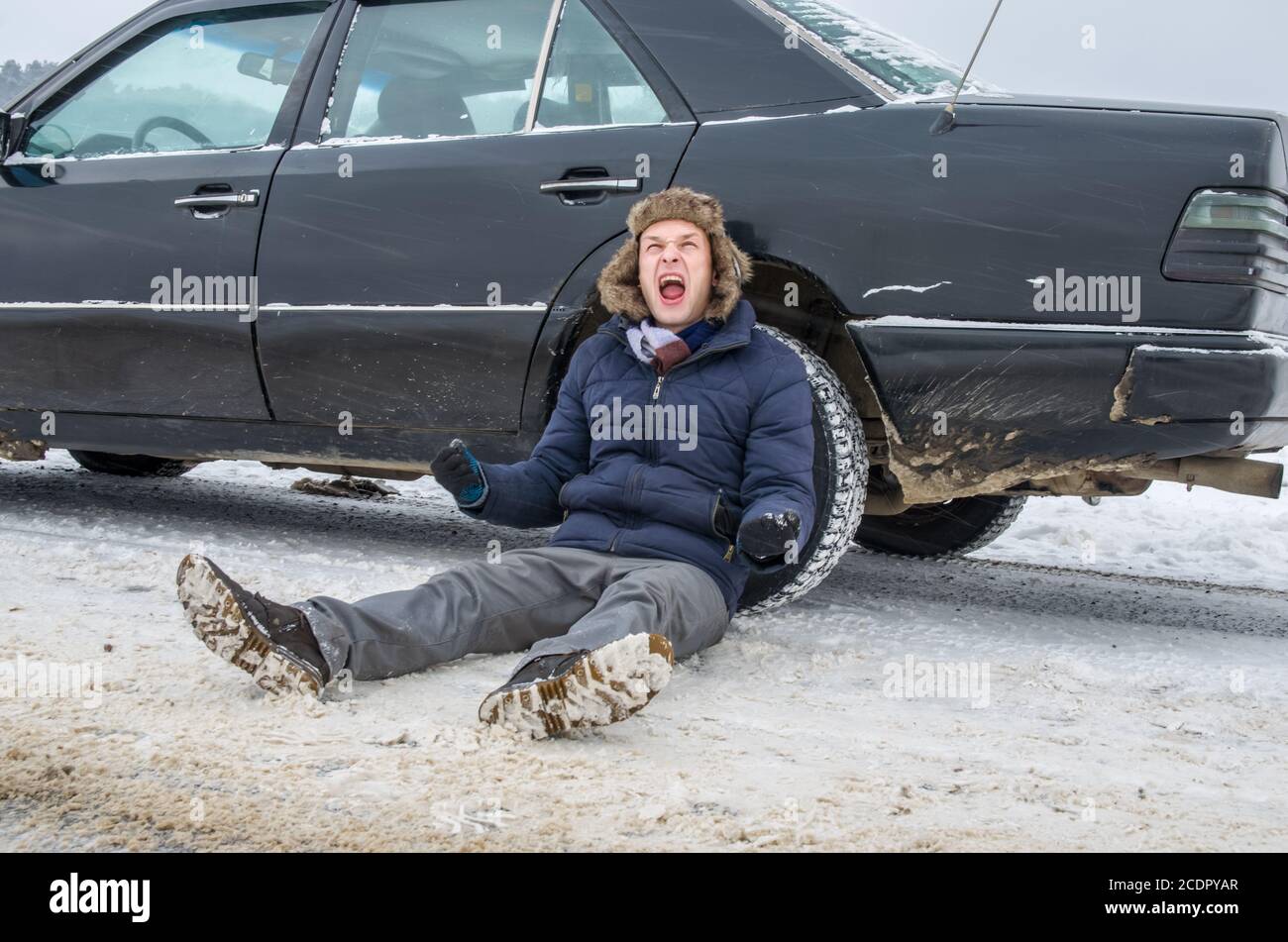Angry young man waiting for help, sitting near a broken car on the side ...