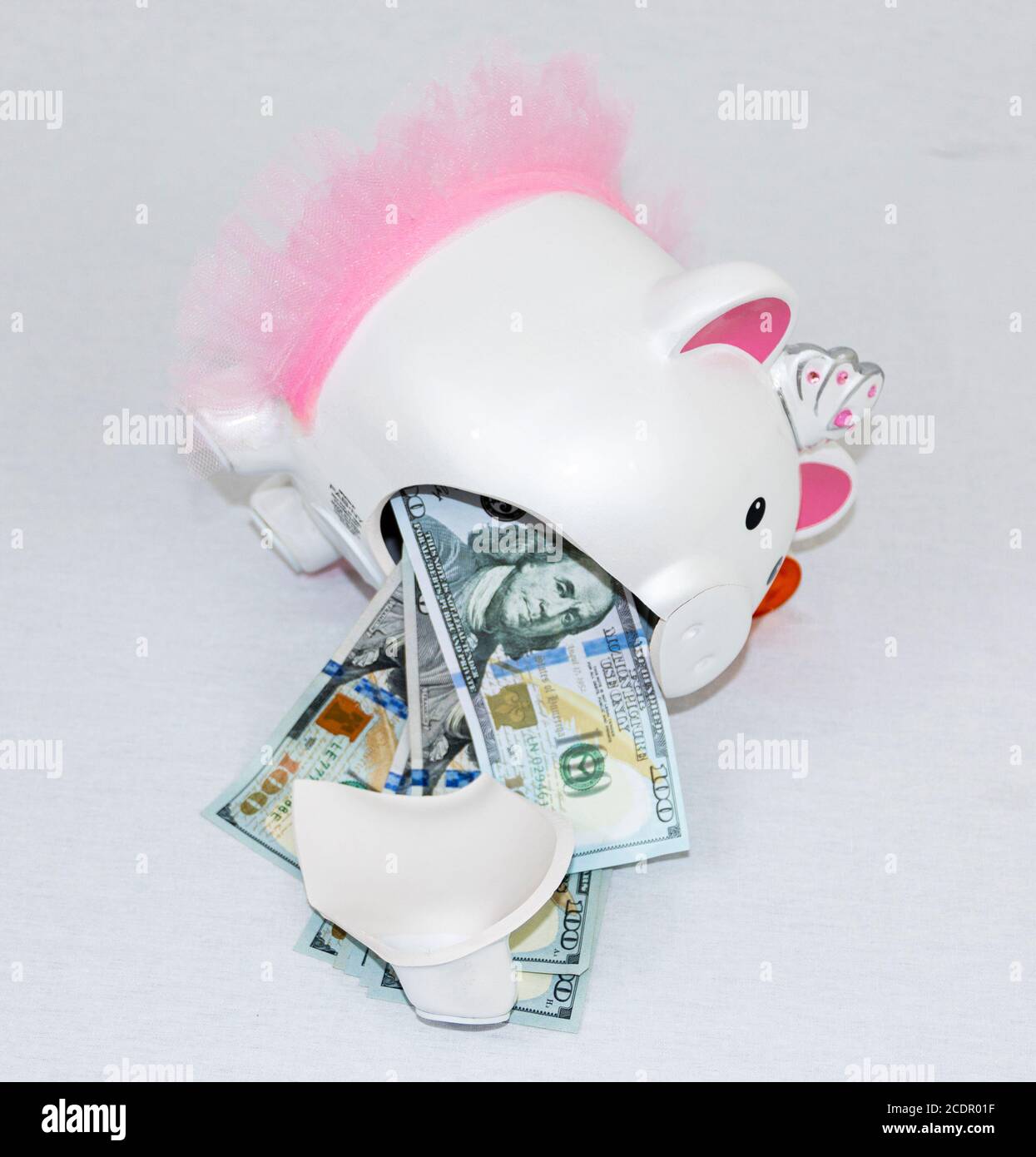 A white piggy bank lying on its side is broken with one hundred dollar ...