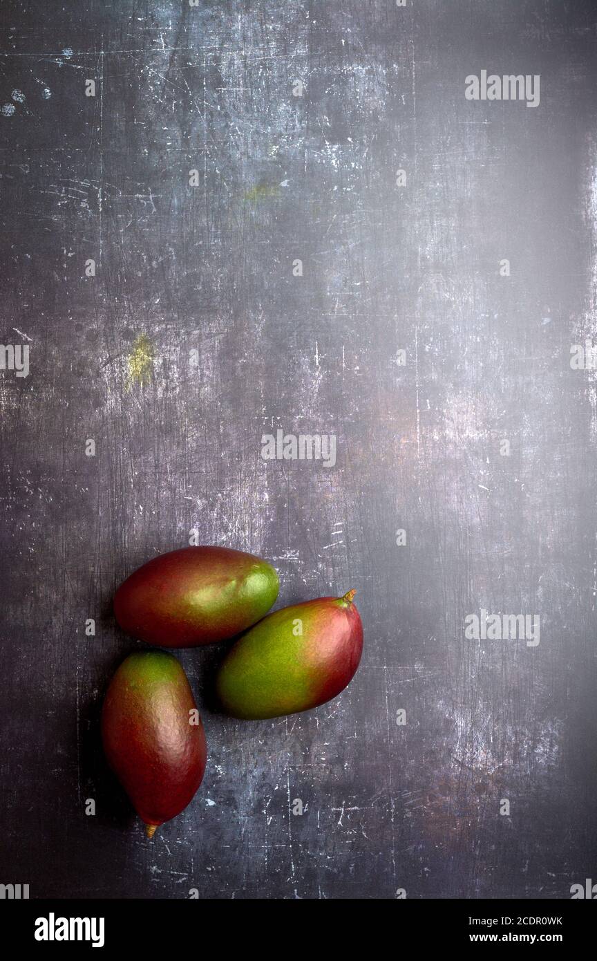 set of mangoes, cut and uncut, on a black, dark, metallic, cement ...