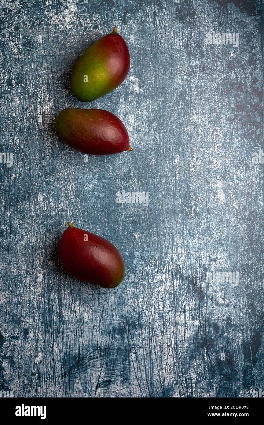 set of cut and uncut mangoes, on a dark, blue, cement, metal, marble ...