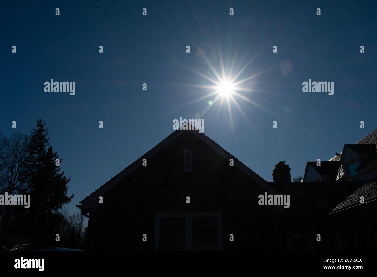 A Bright Sun Over a Silhouetted Suburban Building and Trees Stock Photo ...