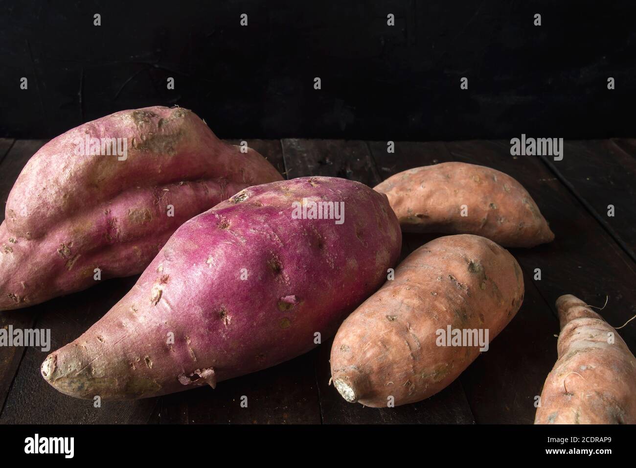 Red colored raw sweet potatoes on dark rustic backdrop Stock Photo - Alamy