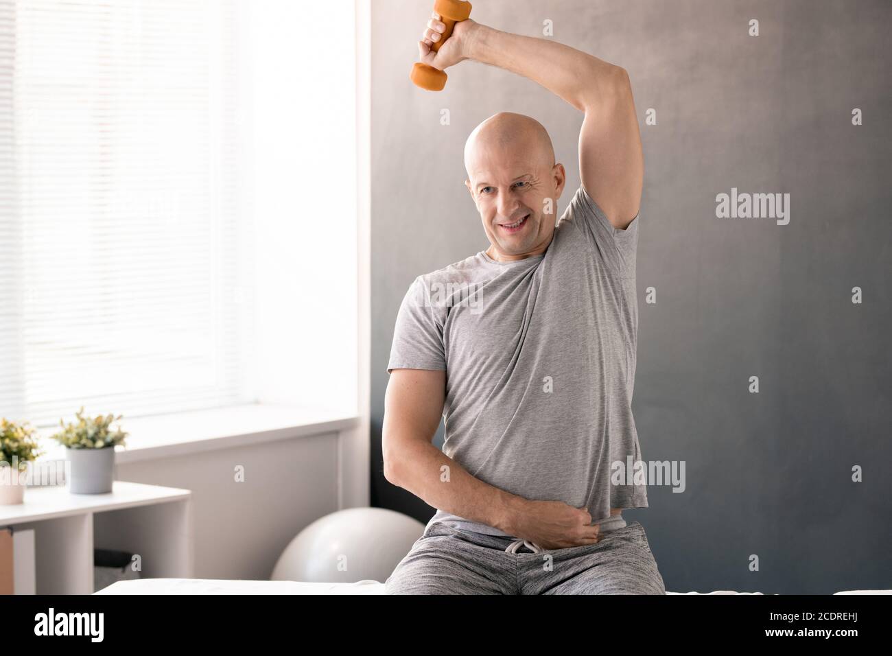 Bald middle aged man in activewear doing physical exercise with ...