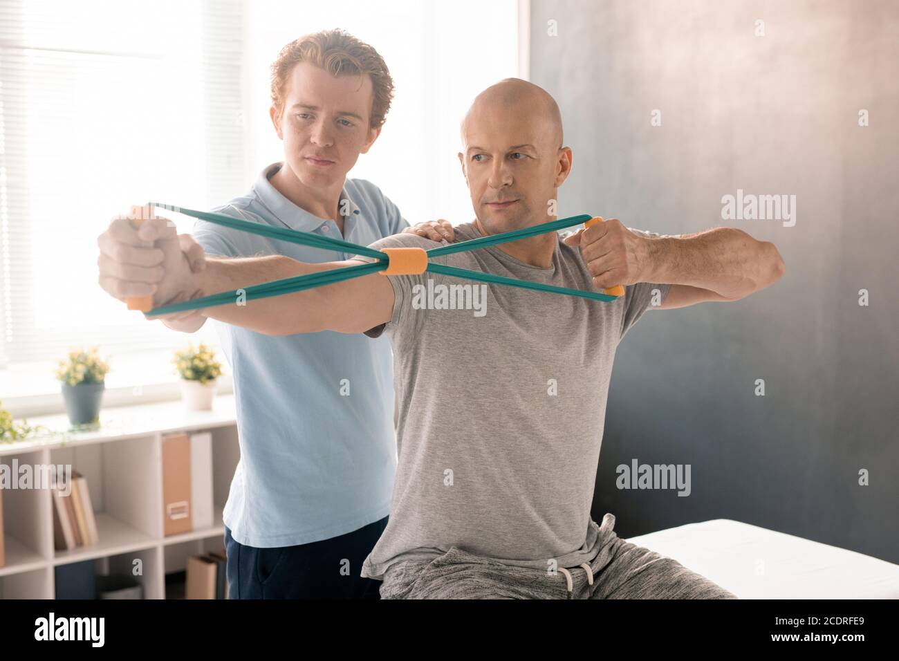 Bald middle aged man stretching resistance band during exercise for ...