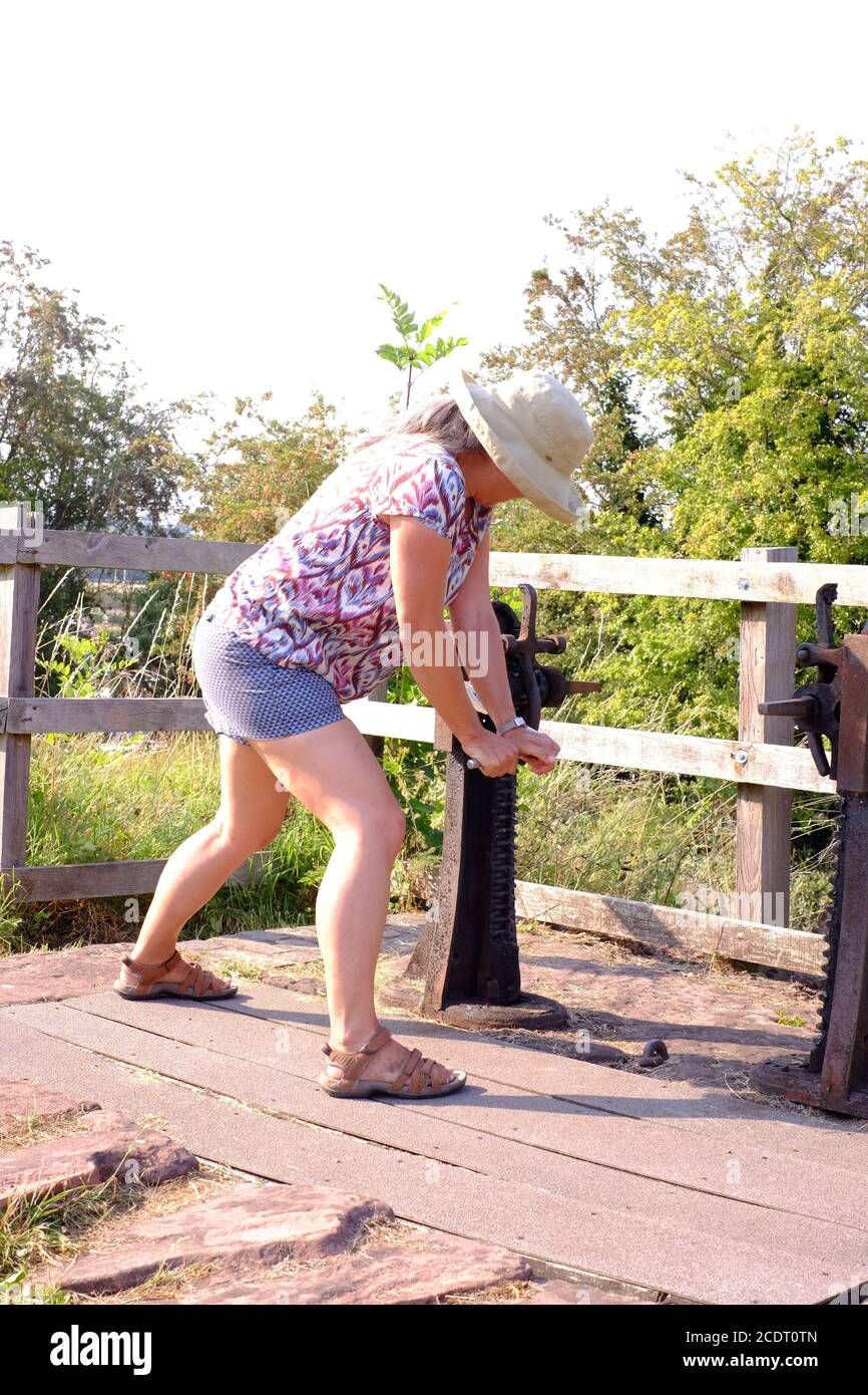 Woman operating canal lock using a windlass tool to move lock gate ...