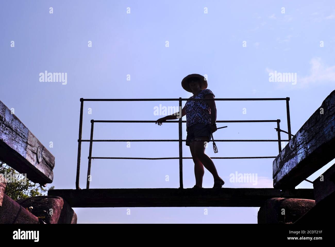 Woman operating canal lock using a windlass tool to move lock gate ...