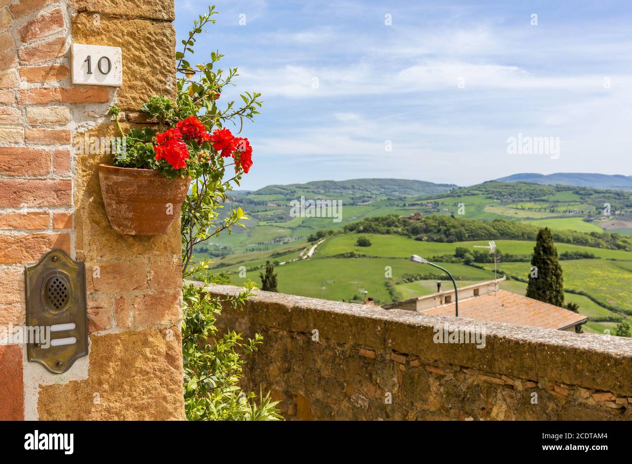 Red flowers in a flower pot on a wall with view the Tuscan landscape in ...