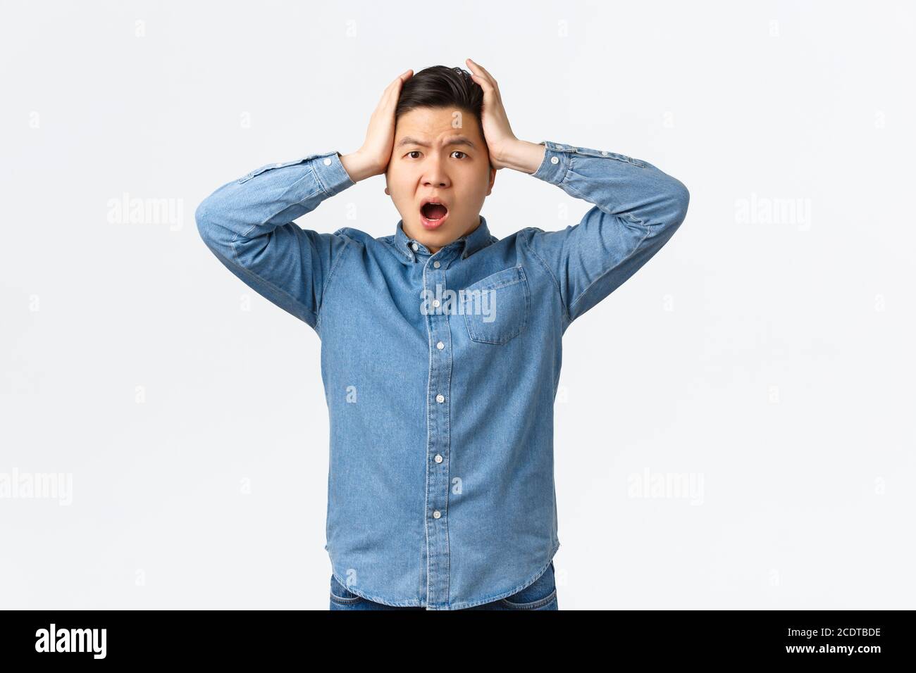 Shocked and concerned asian man grab head and shaking it in panic and ...