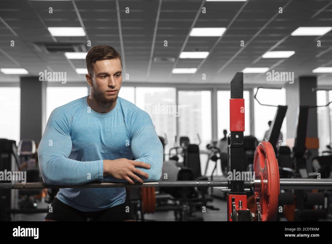 A handsome male bodybuilder is resting after exercising in the gym ...