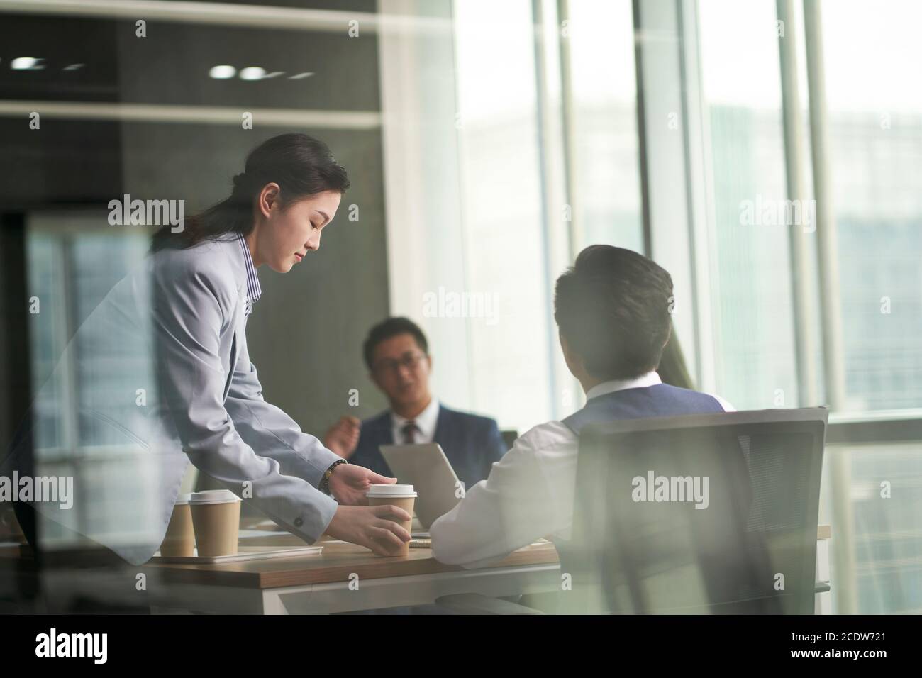 through-the-glass shot of a young asian intern trainee bringing coffee ...