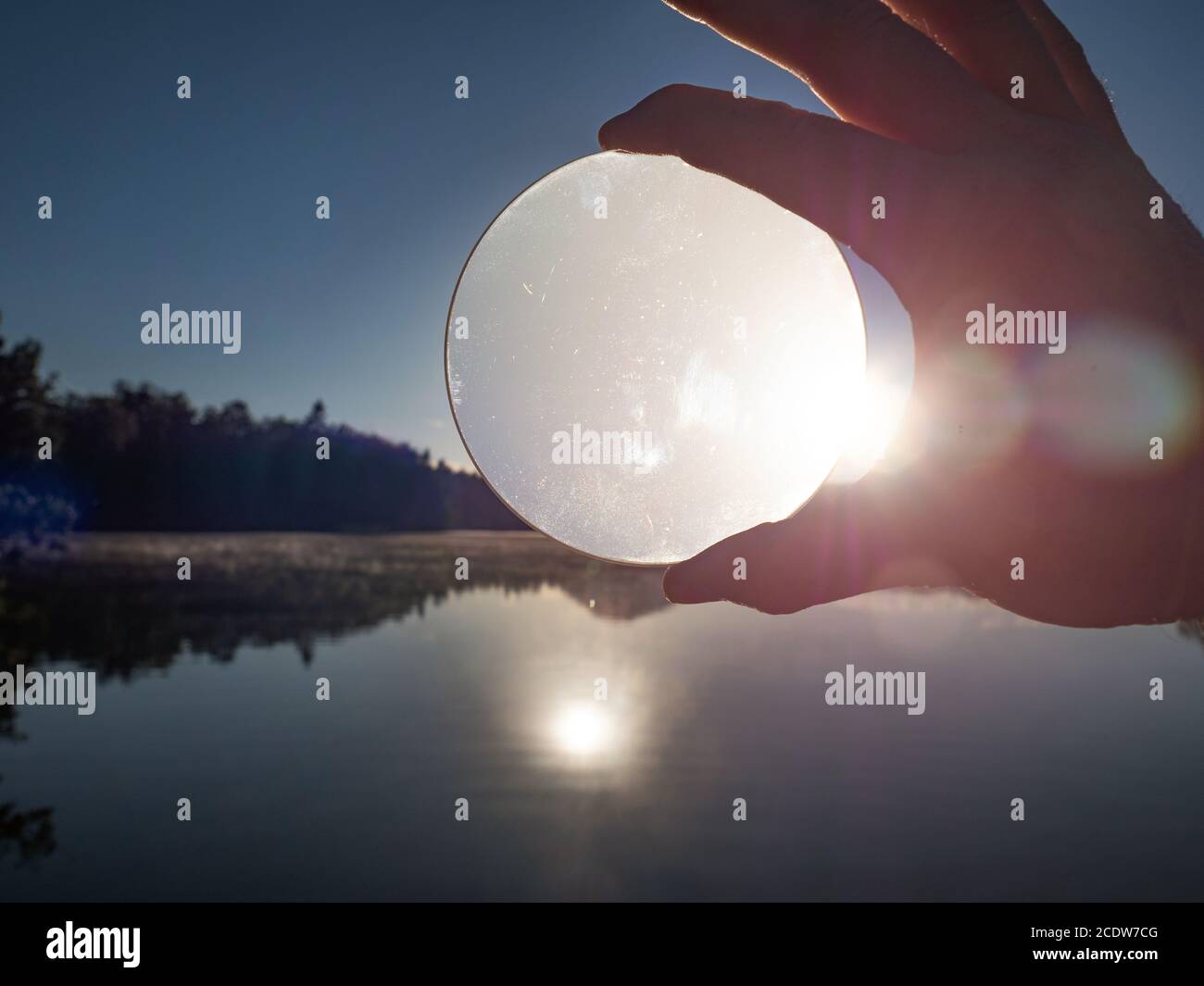 Hand hold glass lens or ball uniquely reflects summer lake scene with ...