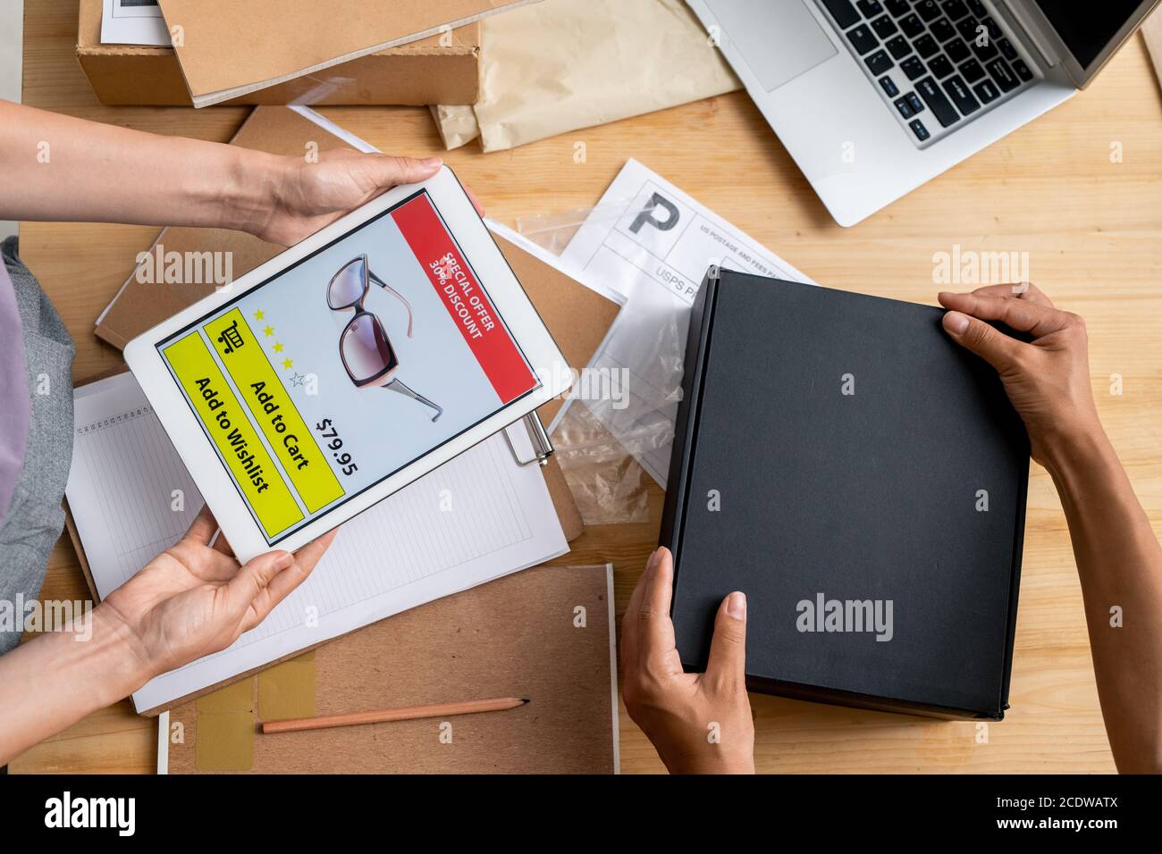 Hands of managers of online shop holding tablet and packing box with ...