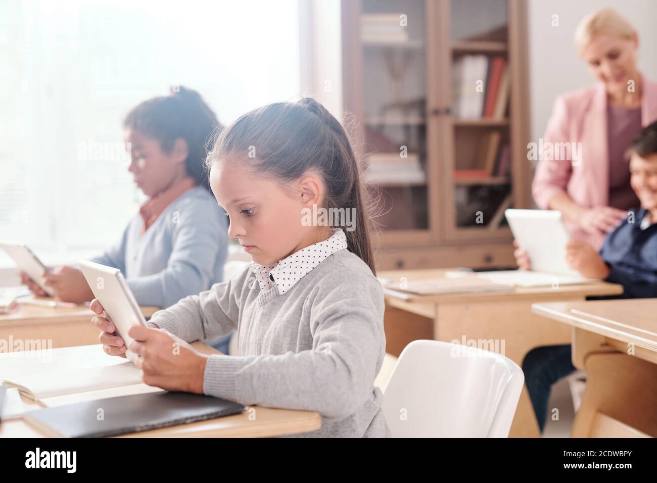 Serious clever girl and her classmates with tablets working ...