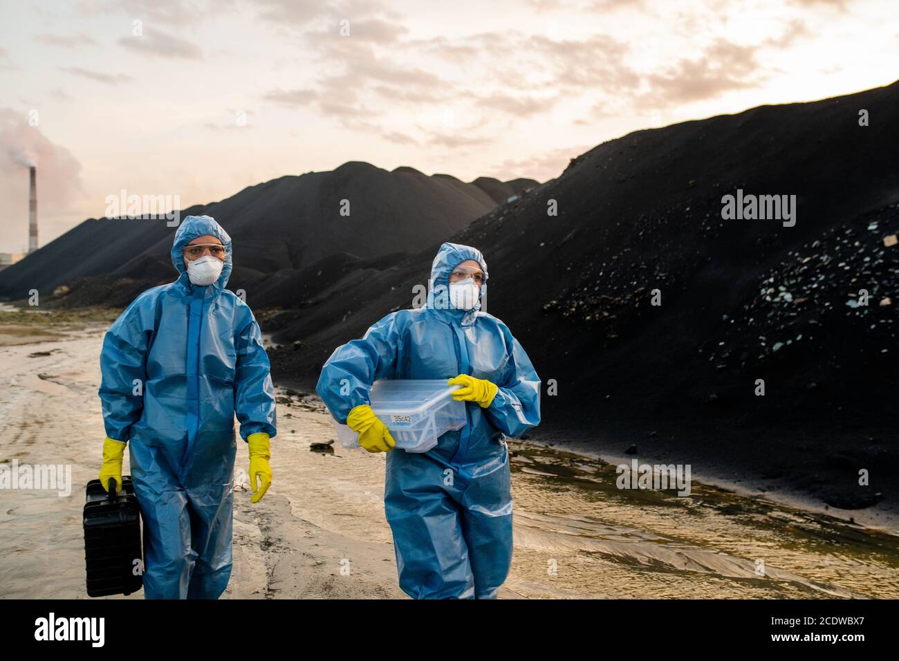 Two female ecologists in coveralls, respirators, eyeglasses and rubber ...