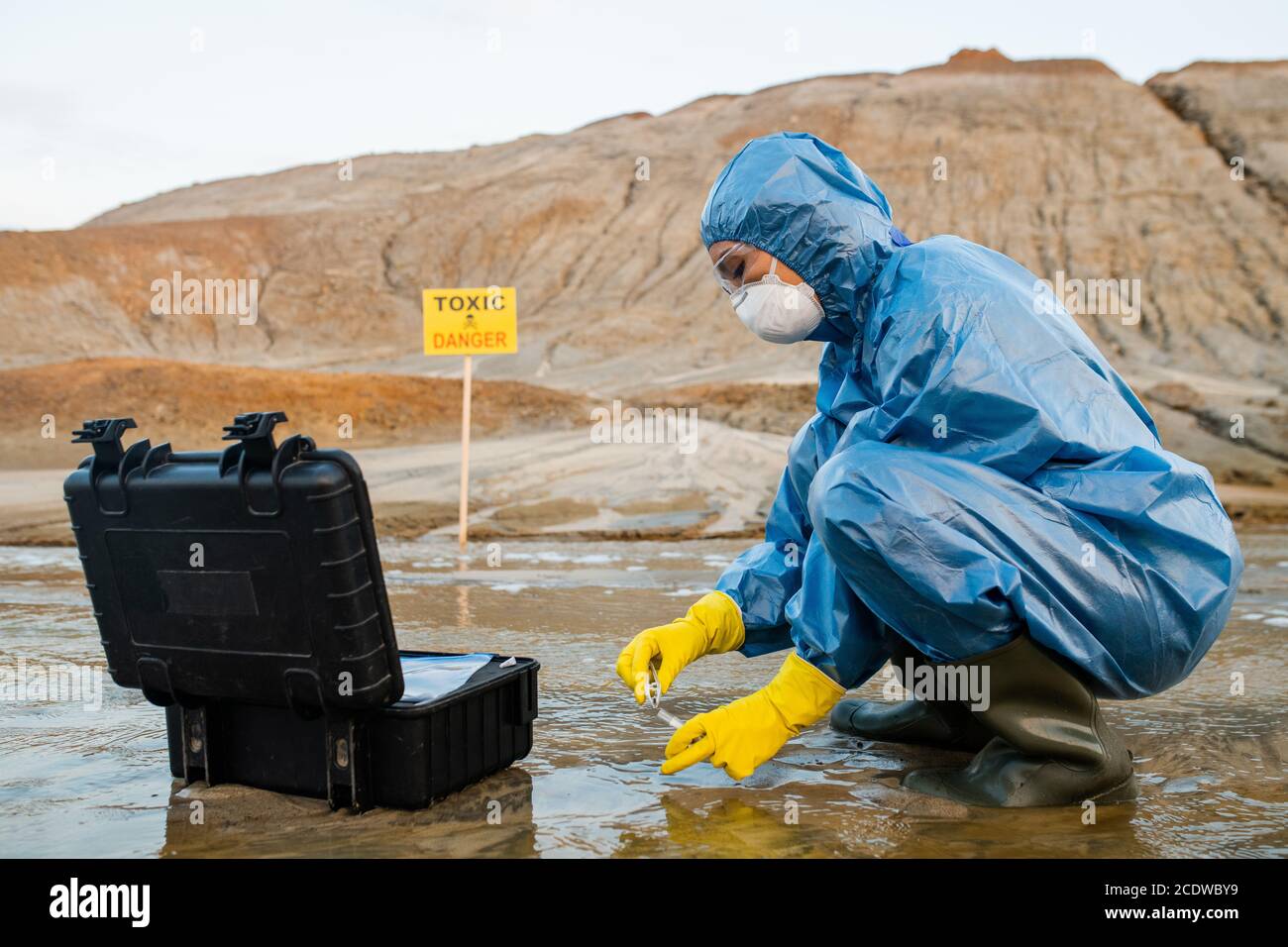Contemporary young female ecologist putting sample of water into flask ...