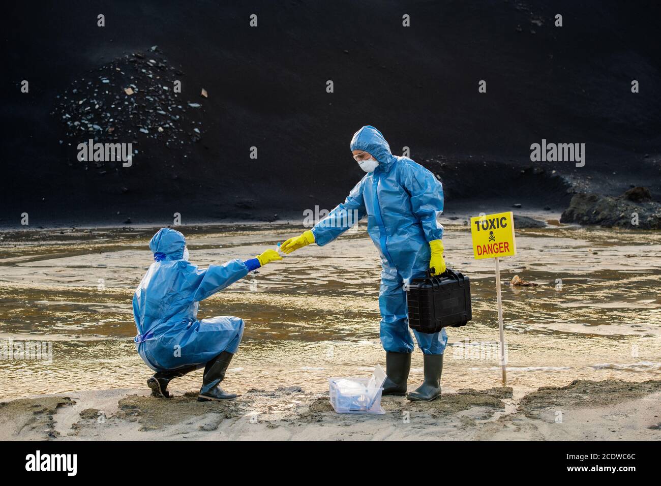Young ecologist in protective workwear taking flask with sample of ...