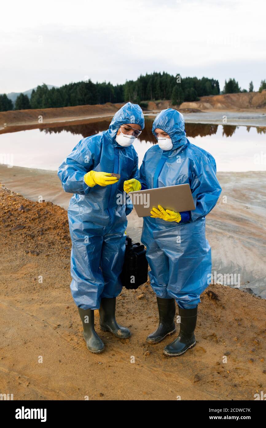 Young female ecologists in protective workwear standing on polluted ...