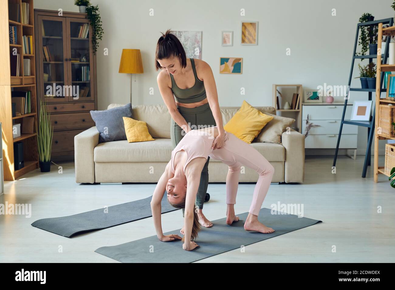 Young active woman helping her teenage daughter during backbend ...