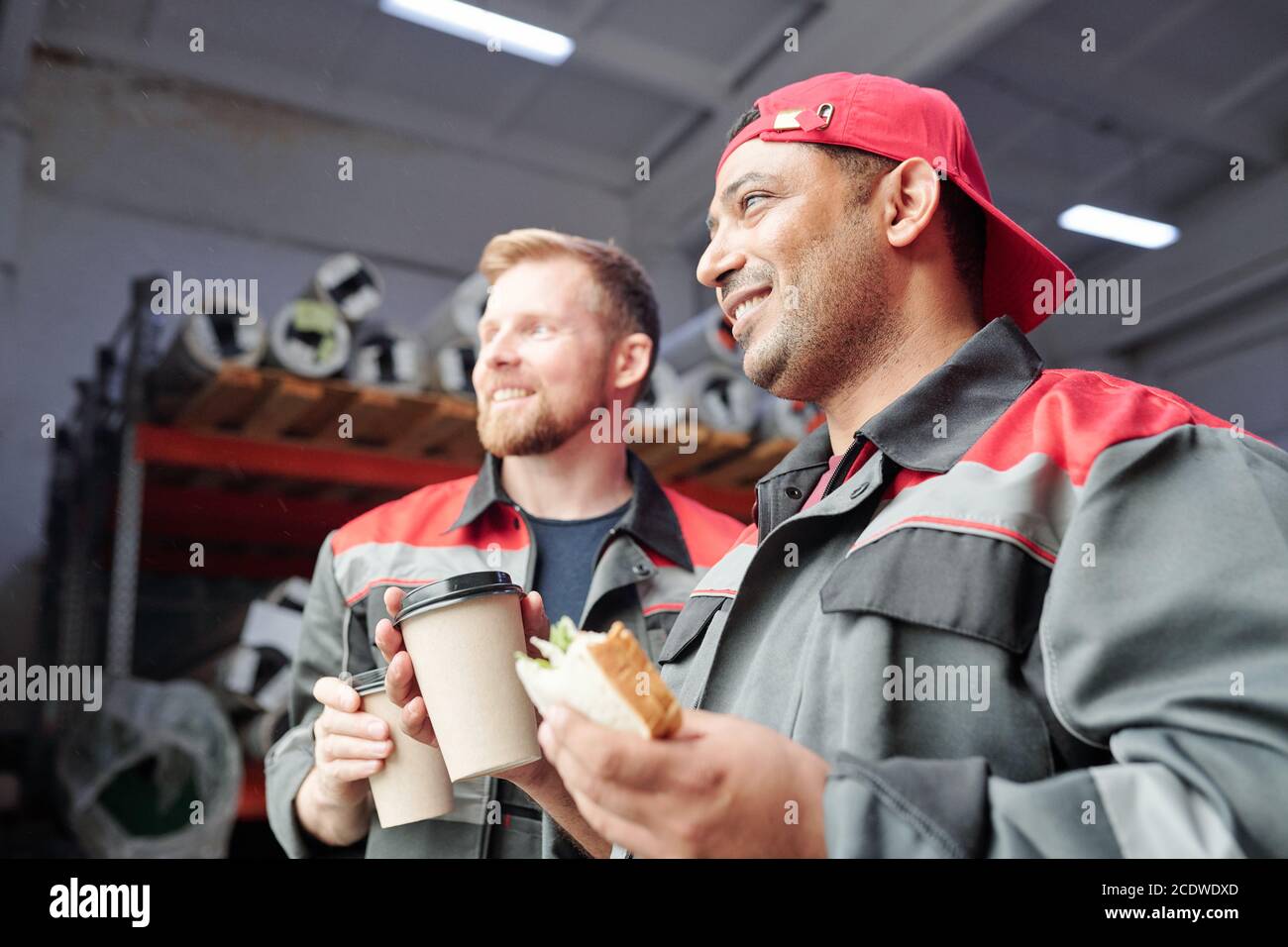 Two happy young intercultural male workers with sandwiches and coffee ...