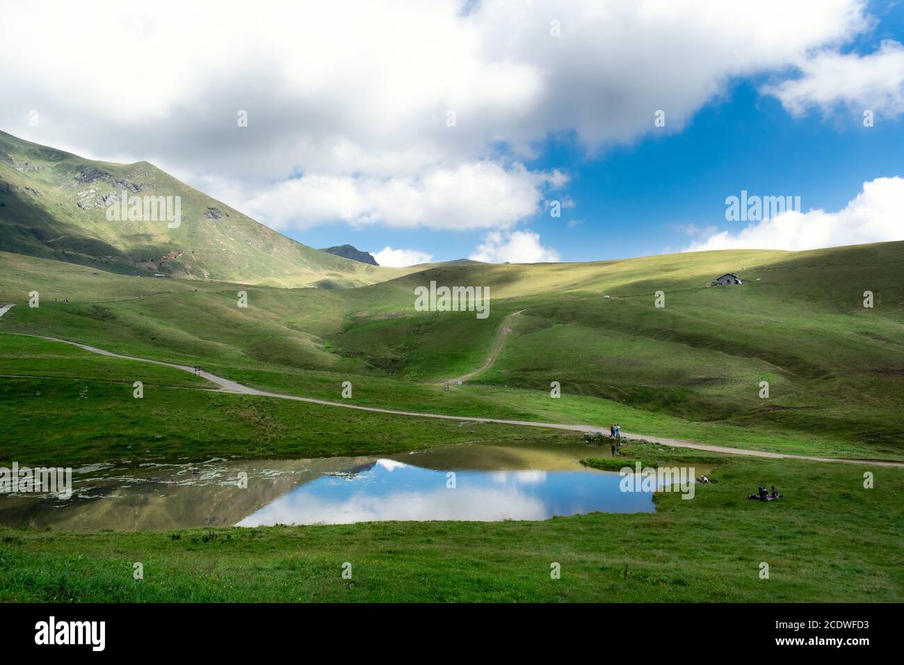 Grassy plateau crossed by a path, blue sky with stormy clouds, a lake ...